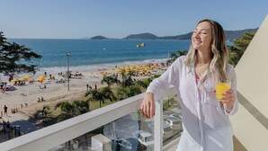Uma varanda com vista para a praia, um copo de suco de laranja e um céu azul e límpido.