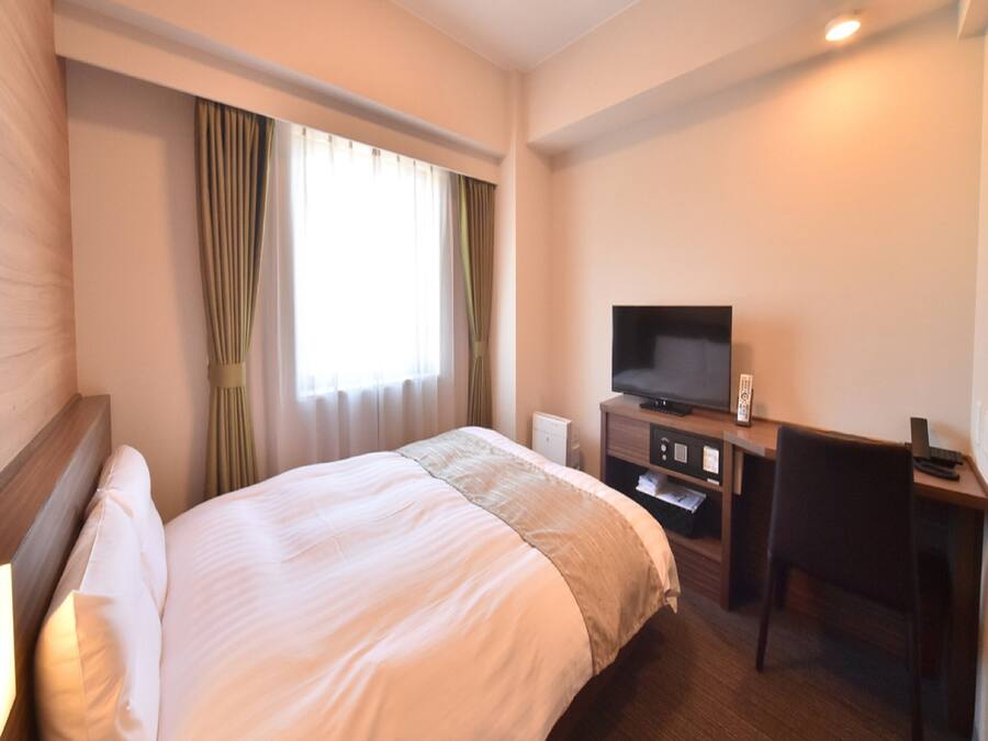 Quarto de hotel com uma cama grande, uma escrivaninha com televisão e uma cadeira.