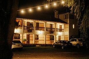 Um edifício de dois andares com varanda, luzes de festa e carros estacionados.