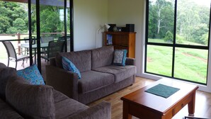 Sala de estar com sofá cinza, mesa de centro de madeira e área de jantar com mesa e cadeiras de vidro.