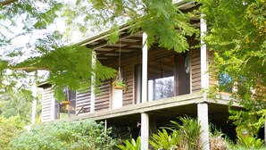 Uma casa de madeira com varanda coberta, janelas amplas e vasos suspensos.