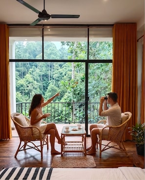 Quarto com amplas janelas, mobiliário de vime e vista para uma floresta.