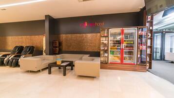 Um saguão de hotel com cadeiras de massagem, um espaço de estar e uma geladeira abastecida com bebidas.