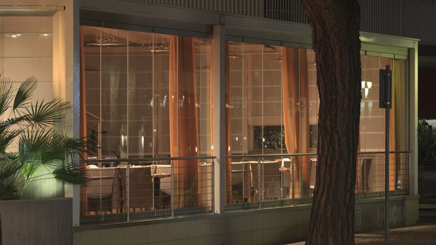 Um restaurante com grandes janelas de vidro, móveis de vime e uma árvore em frente.