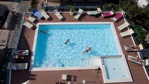 Piscina no terraço com vários espreguiçadeiras e uma piscina menor ao lado.