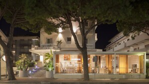 Um hotel com fachada de vidro, área de estar externa e escadaria que leva à entrada.