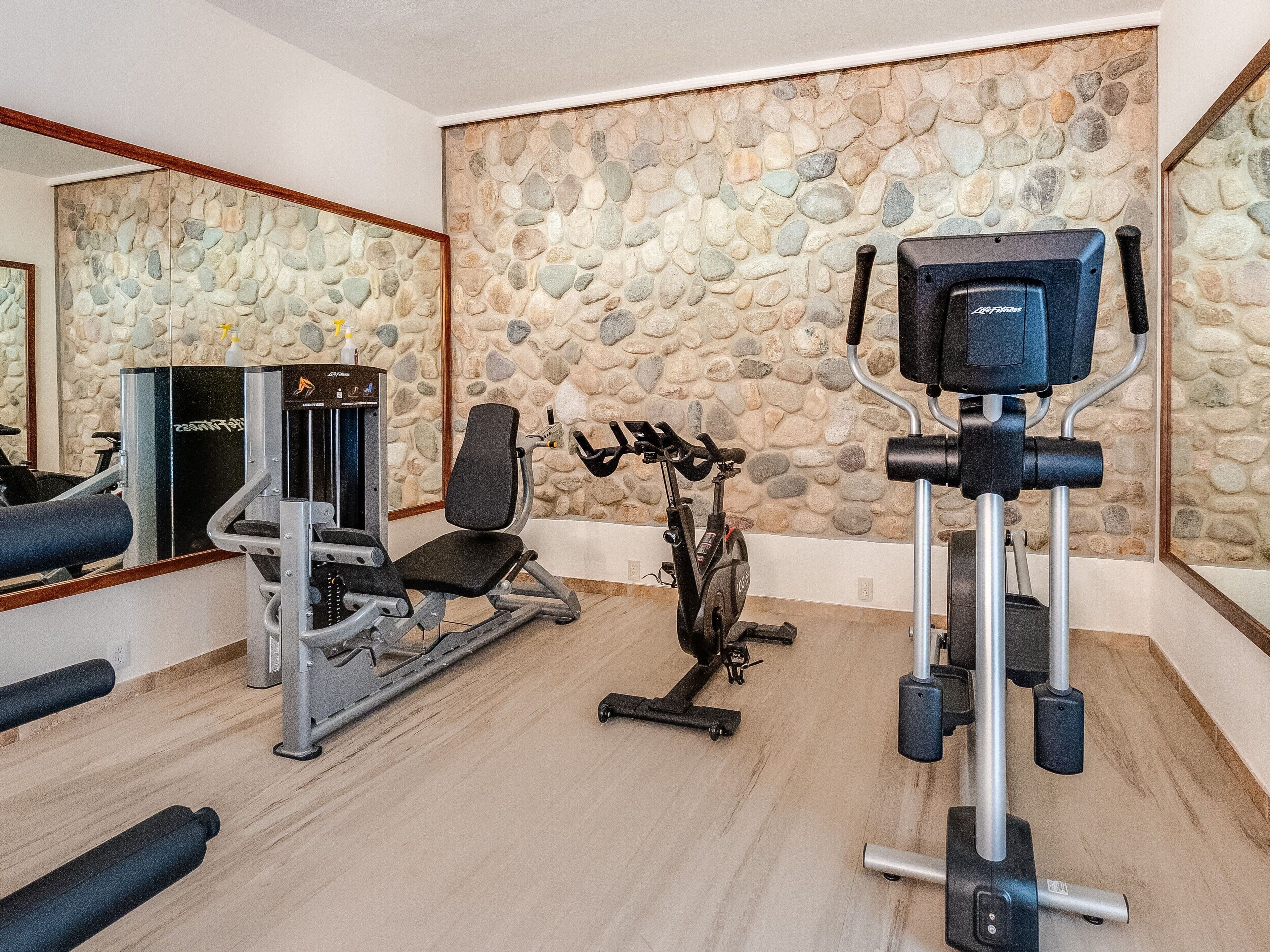 Uma academia em casa com equipamentos de ginástica, uma parede de pedra e um espelho.