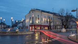 Um hotel com fachada vermelha e branca, numa esquina, com um restaurante visível.