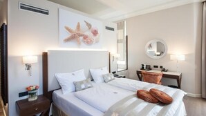 Quarto de hotel com uma cama grande, mesas de cabeceira, uma escrivaninha, um espelho e um quadro de estrela-do-mar na parede.