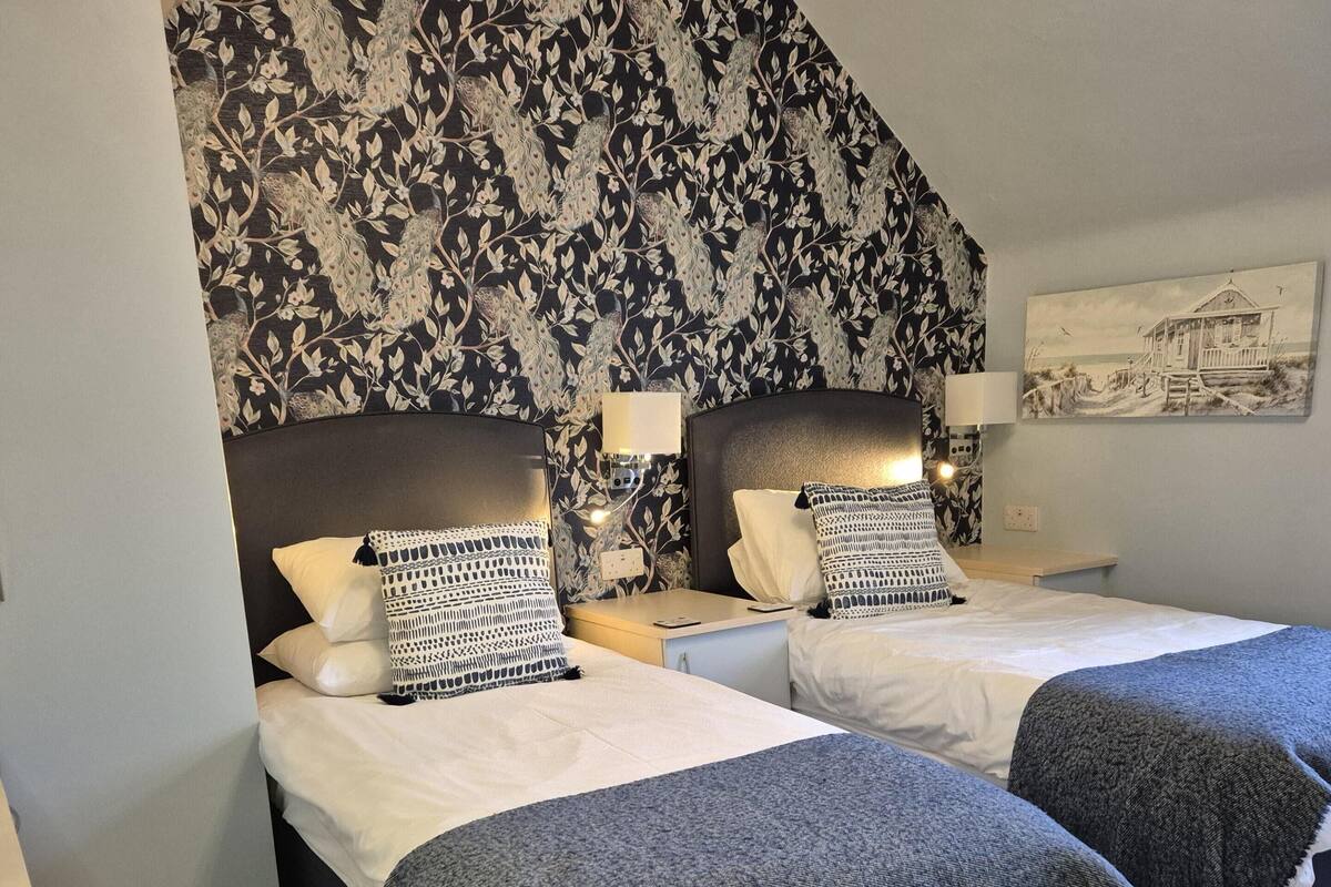 Quarto com duas camas, cada uma com cabeceira, abajures laterais e papel de parede estampado.