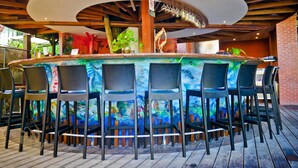Uma área de bar com teto de madeira, um mural na parede e várias cadeiras pretas ao redor.