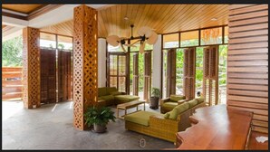 Amplo espaço interno com ventilador de teto, móveis de madeira e janelas grandes que permitem entrada de luz natural.