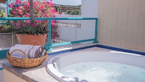 Uma varanda com hidromassagem, um cesto de vime com toalhas e um vaso grande com flores cor-de-rosa.