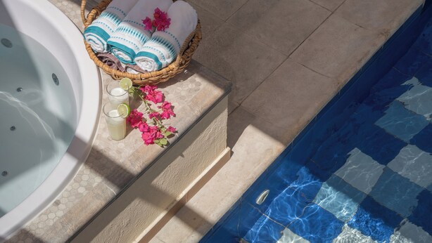 Uma área ao lado da piscina com hidromassagem, uma cesta de toalhas e um copo de bebida.