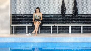 Mulher sentada à beira da piscina, com parede estampada e degraus revestidos em azulejo.