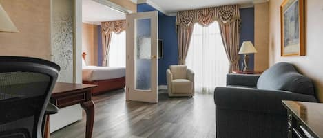 Quarto de hotel com uma cama, uma escrivaninha, uma cadeira, um sofá e uma luminária.