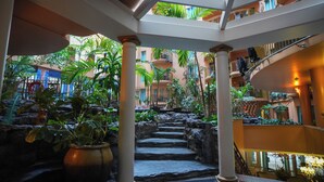 Um átrio com vários níveis e uma escadaria central, cercado por vegetação exuberante e plantas tropicais.