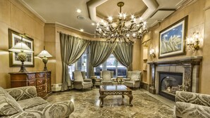 Uma sala de estar luxuosa com um candelabro, lareira e vista da cidade através de grandes janelas.