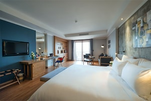 Quarto de hotel moderno com uma cama grande, uma escrivaninha com cadeira, televisão e uma janela ampla.
