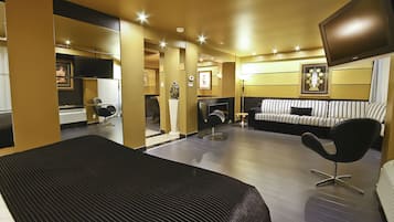 Quarto de hotel moderno com uma cama grande, um sofá listrado, uma cadeira preta e uma televisão de tela plana.