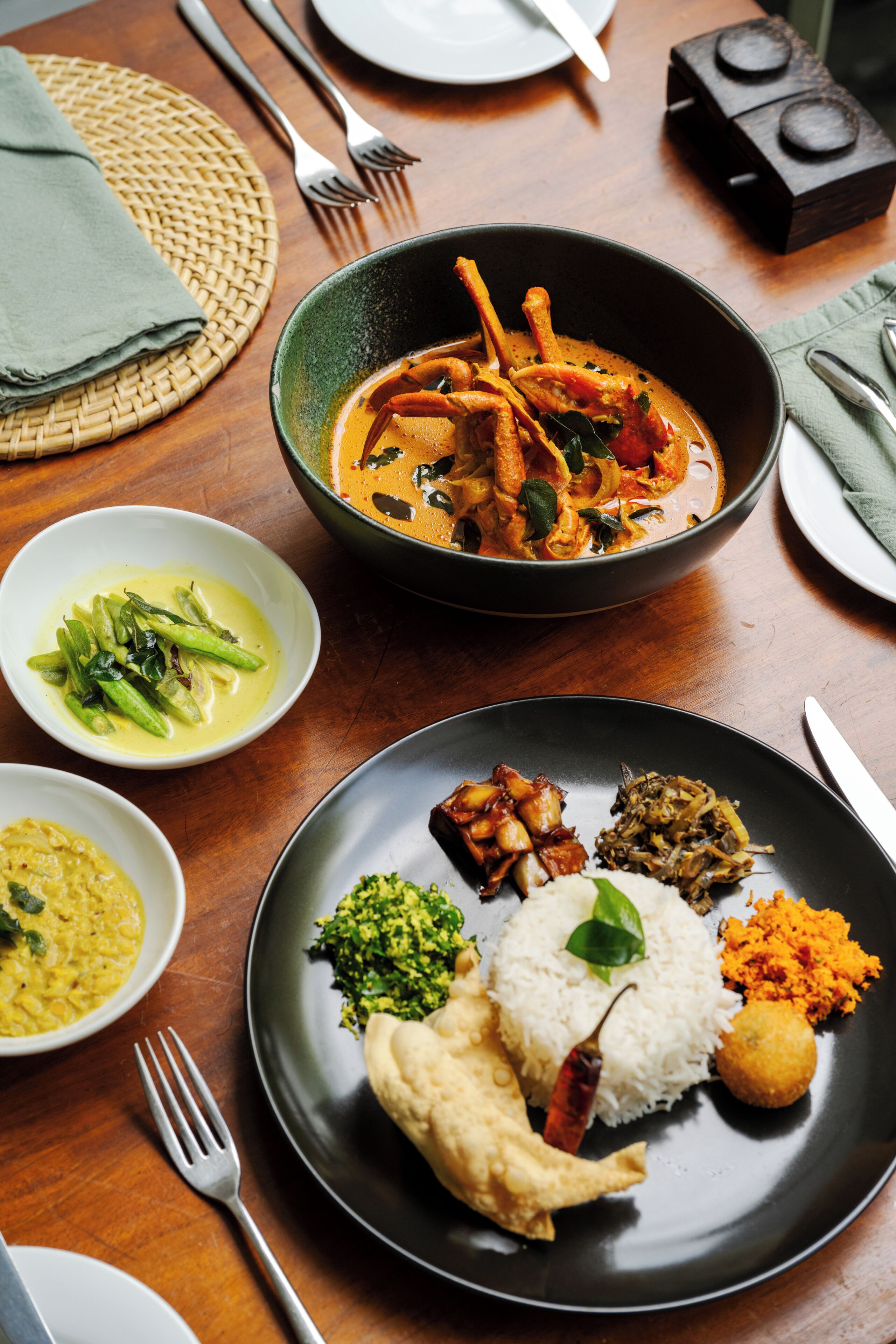 Uma mesa com diversos pratos, incluindo um tacho de curry, um prato de arroz, vegetais e um item frito.