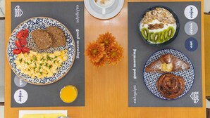 Mesa de café da manhã com pratos de comida, uma xícara de café e um vaso de flores.