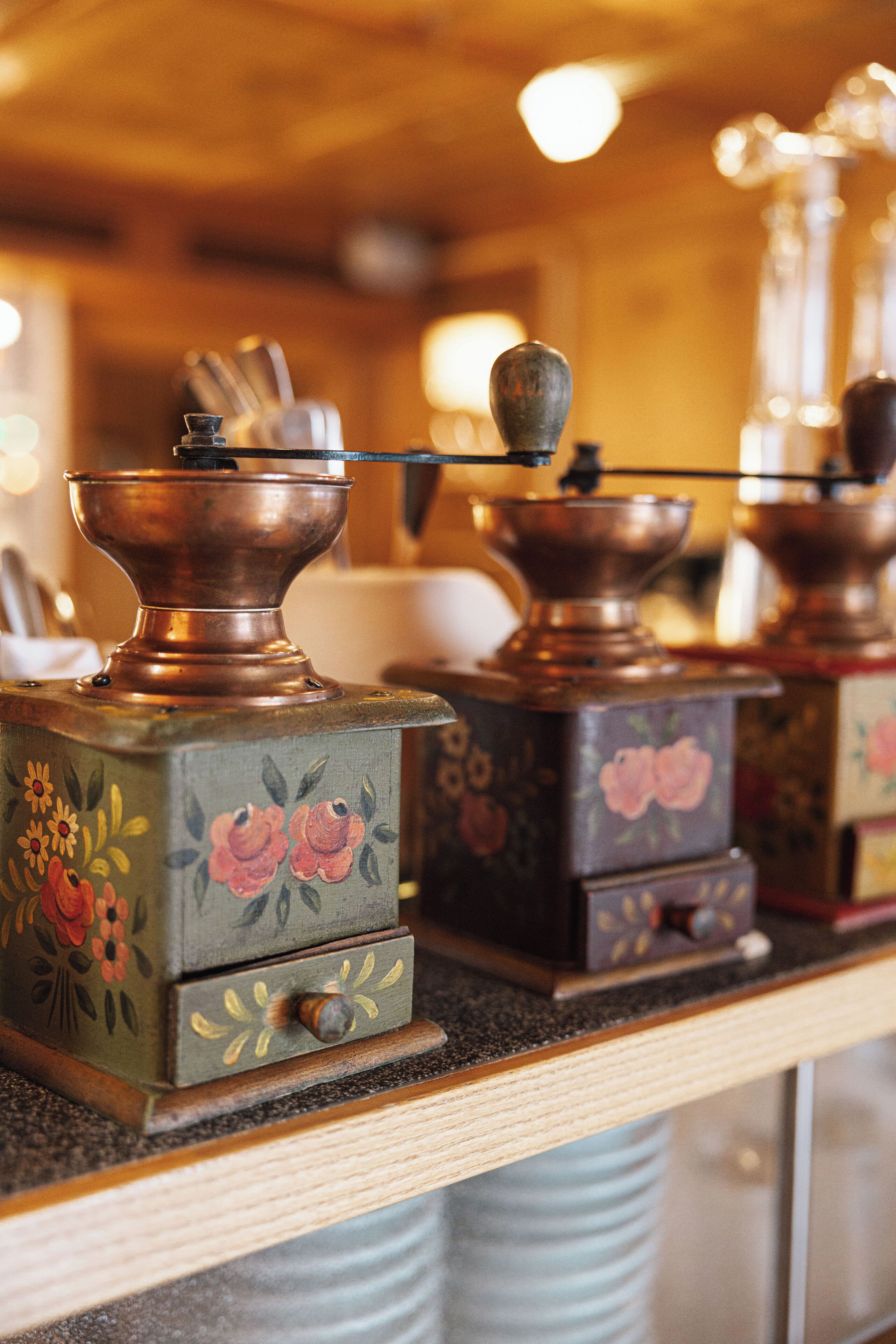 Uma fileira de moedores de café antigos com desenhos florais sobre uma prateleira de madeira.