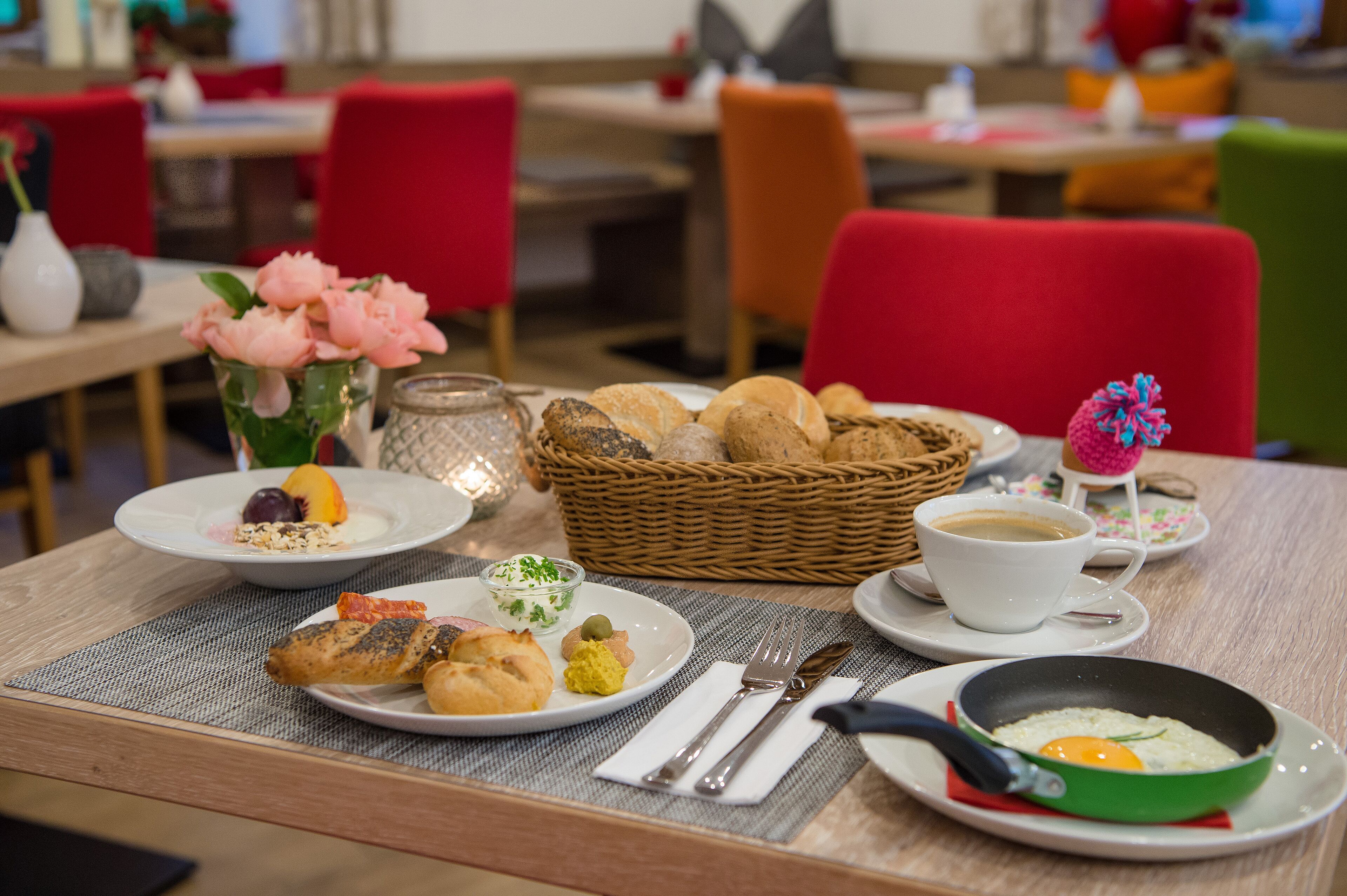 Mesa de café da manhã com diversos pratos, incluindo ovos, doces e uma xícara de café.