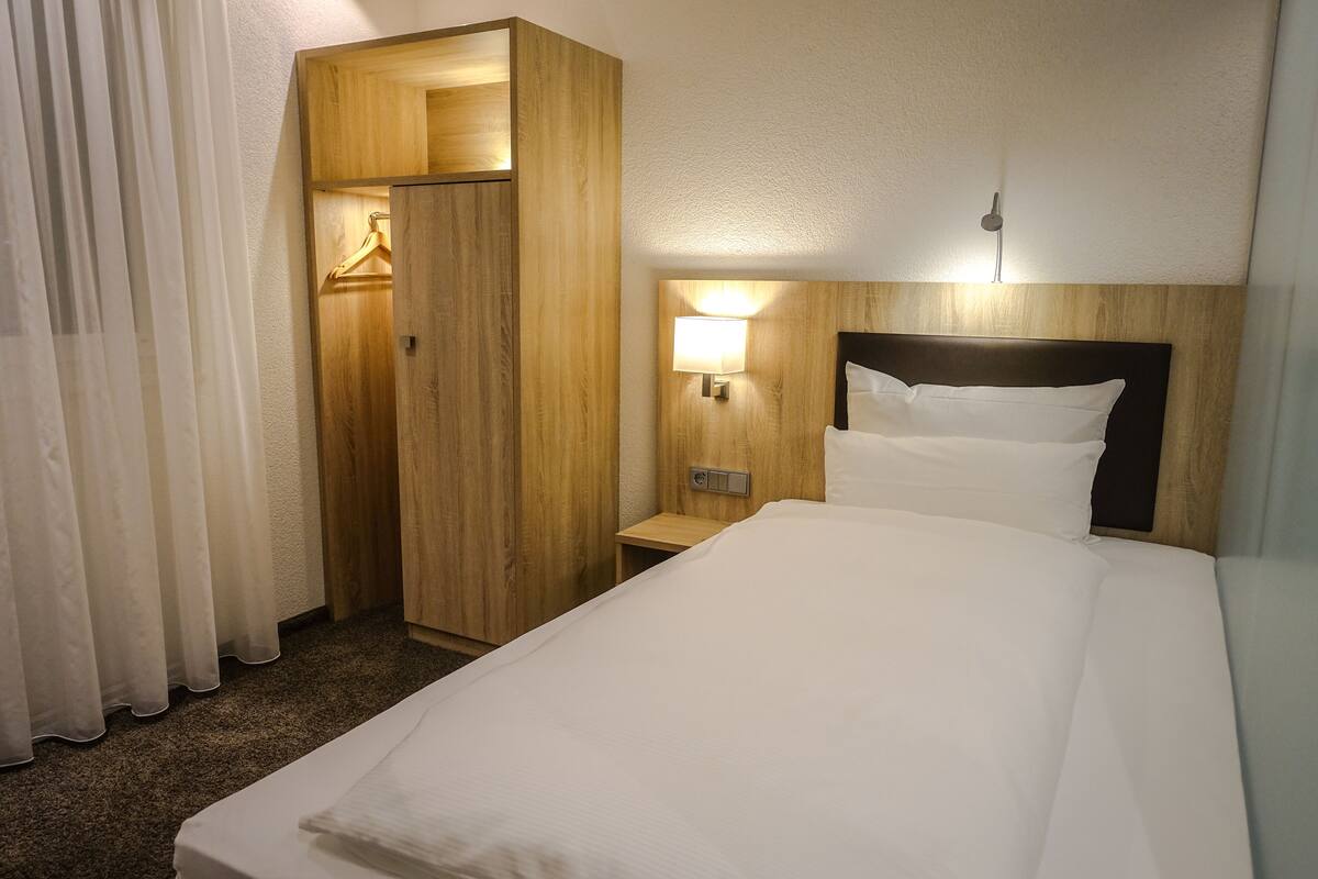 Quarto de hotel com uma cama grande, guarda-roupa de madeira e mesa de cabeceira com abajur.
