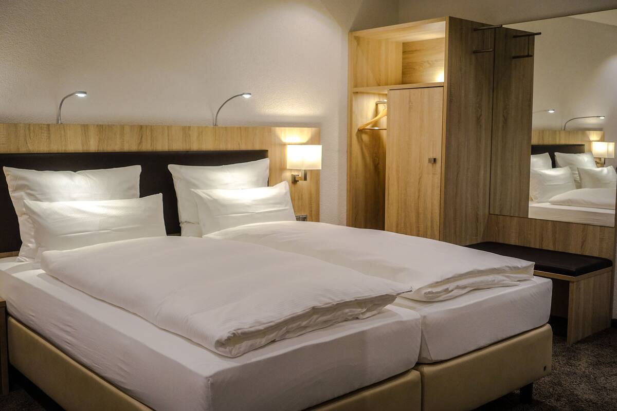 Uma cama de casal com cabeceira de madeira, luminárias de cabeceira, um guarda-roupa de madeira e um espelho.