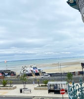Vista costeira com praia, posto de salvação marítima e passarela para pedestres.