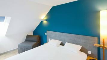 Quarto de hotel com uma cama, um pequeno sofá, uma mesa de cabeceira e uma luminária.