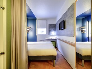 Quarto de hotel com duas camas, banheiro, televisão e janela.