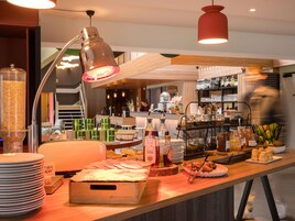 Disposição de buffet com diversos alimentos, um espaço para bebidas e um bar ao fundo.