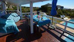 Uma área de estar coberta ao ar livre com mesa posta para refeições, piscina e vista para a paisagem circundante.