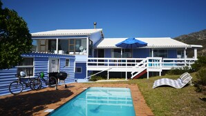 Uma casa de dois andares com piscina, um deck coberto e uma bicicleta estacionada na frente.