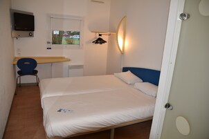 Quarto com cama, escrivaninha, cadeira, televisão e janela.