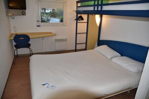 Uma cama beliche com roupa de cama branca, uma mesa com cadeira e uma janela com vista para áreas verdes.