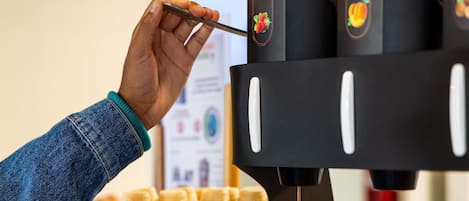 Uma pessoa usando uma máquina de café para preparar uma bebida, com pilhas de copos e uma mesa de madeira à vista.