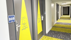 Corredor de hotel com portas identificadas com os números 203 e 205, cada uma com uma placa amarela com a imagem de um gato dormindo e texto em francês.