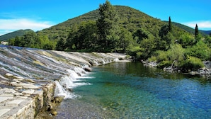 Um rio límpido com leito pedregoso e uma colina ao fundo.