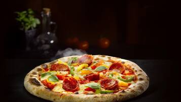 Pizza com pepperoni e vegetais sobre um fundo escuro.