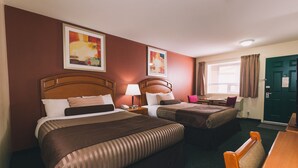 Quarto de hotel com duas camas, uma escrivaninha, uma cadeira, janela com cortinas e obras de arte nas paredes.