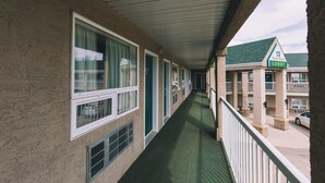 Corredor de hotel com várias divisas, um tapete verde e um guarda-corpo de varanda visível.