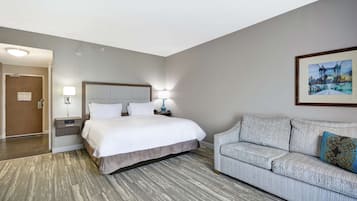 Quarto de hotel com cama, mesa de cabeceira, luminária, sofá e quadro na parede.