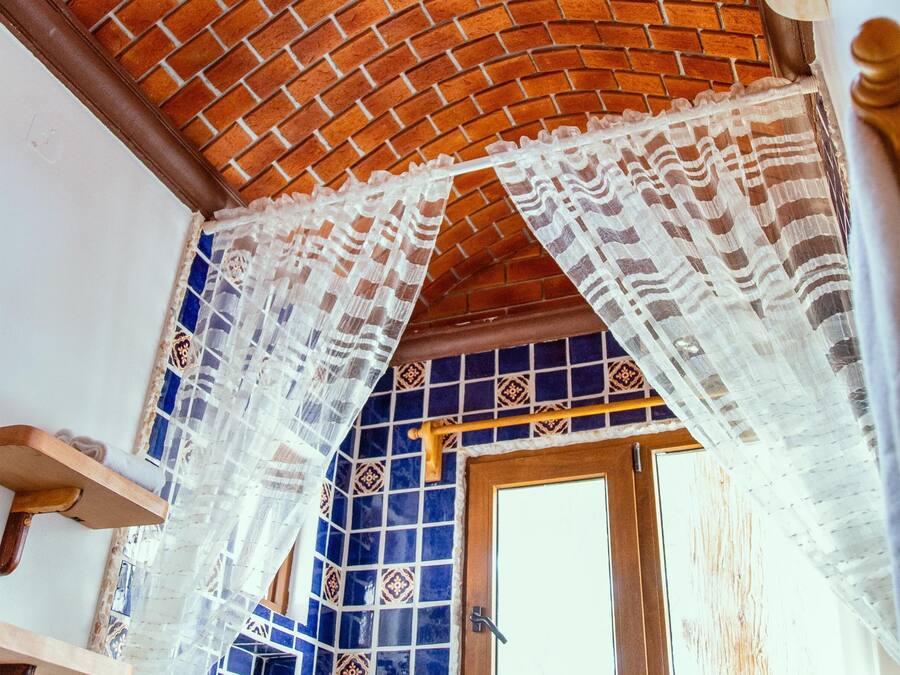 Quarto com chão azul e branco em mosaico, teto de madeira com claraboia circular e janela com moldura de madeira.