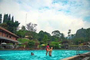 Piscina com pessoas, um gazebo e um edifício com uma placa que diz 'Piscina'.