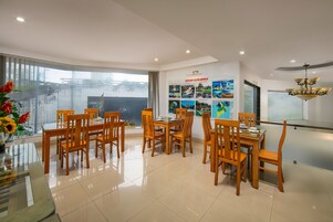 Uma sala de jantar com uma janela grande, cadeiras de madeira, uma mesa de vidro e uma parede com cartazes de viagens.