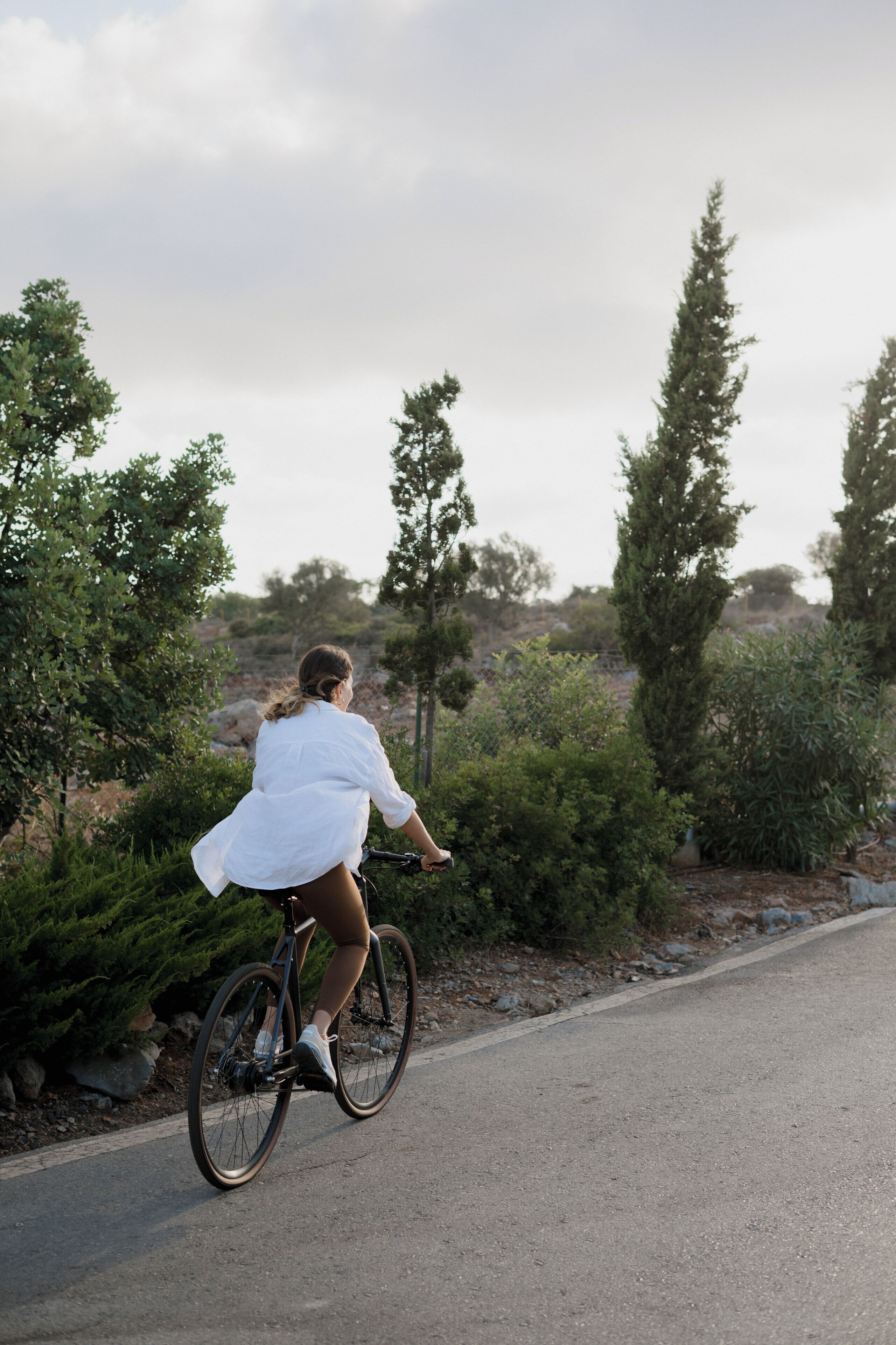 Uma pessoa andando de bicicleta em uma estrada pavimentada, com vegetação nas laterais.