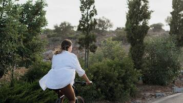 Uma pessoa andando de bicicleta em uma estrada pavimentada, com vegetação nas laterais.